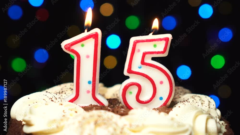 Number 15 on top of cake - fifteen birthday candle burning - blow out at the end. Color blurred ...