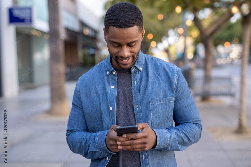 Young black man texting on cell phone walking Stock Photo | Adobe Stock
