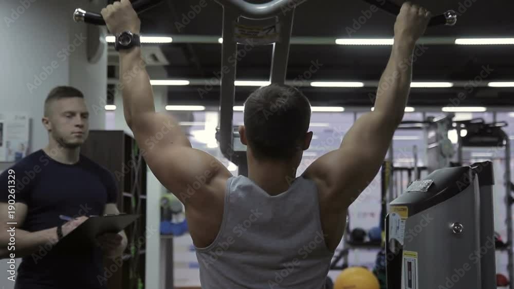 Young athlete is pulling the weight machine in the gym and his male ...