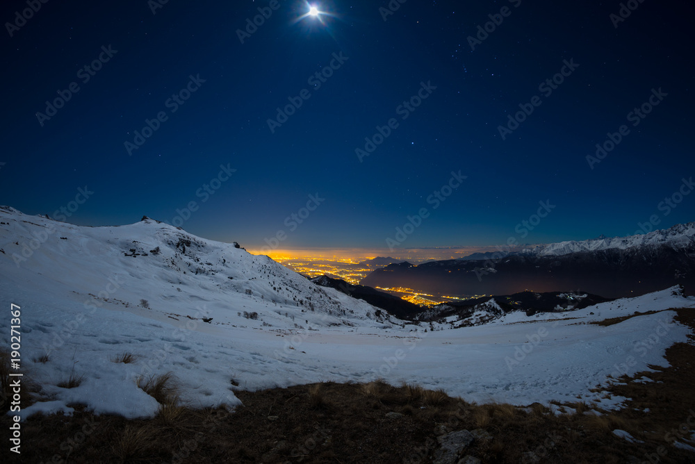 Turin city lights, night view from snow covered Alps by moonlight. Moon and Orion constellation ...