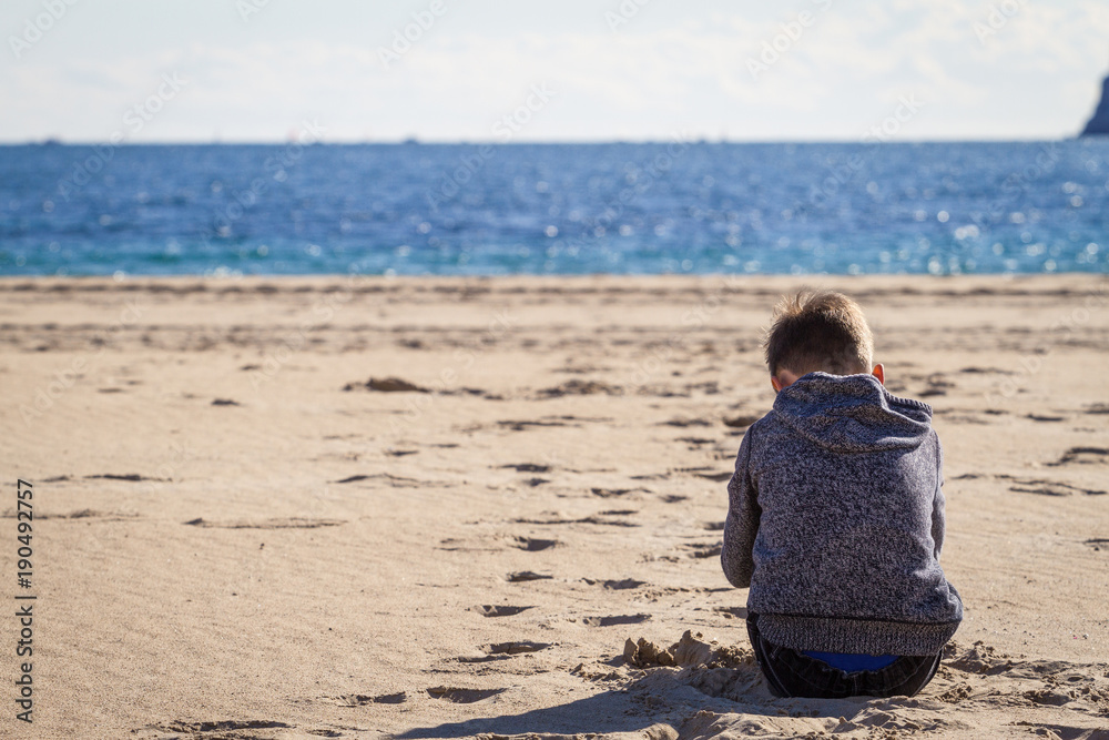 Sad young boy sitting and thinking on the beach Stock Photo | Adobe Stock