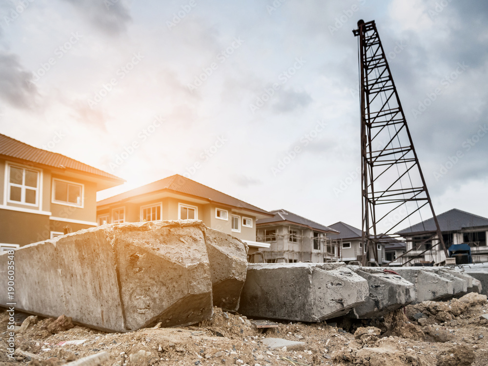 house building at construction site with pile driver and concrete piles ...