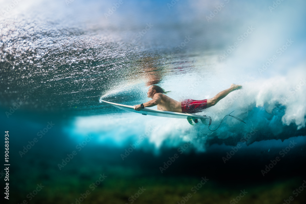 Young surfer dives under the ocean wave with surf board and performs ...