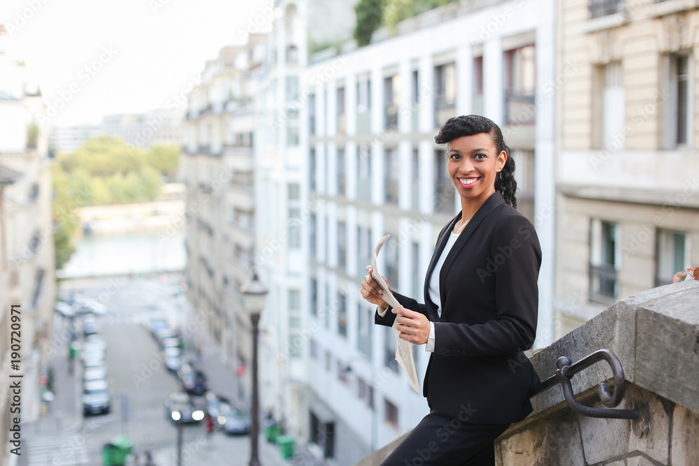 Young reporter looking at cam with newspaper on balcony near high ...