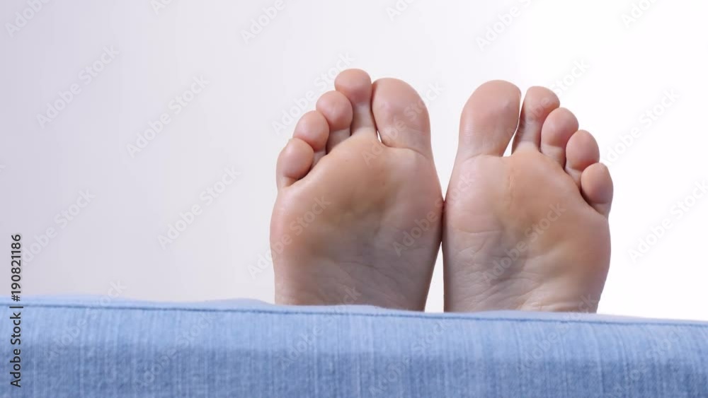 Female resting on sofa showing bare foot. Human feet moving on bed in ...