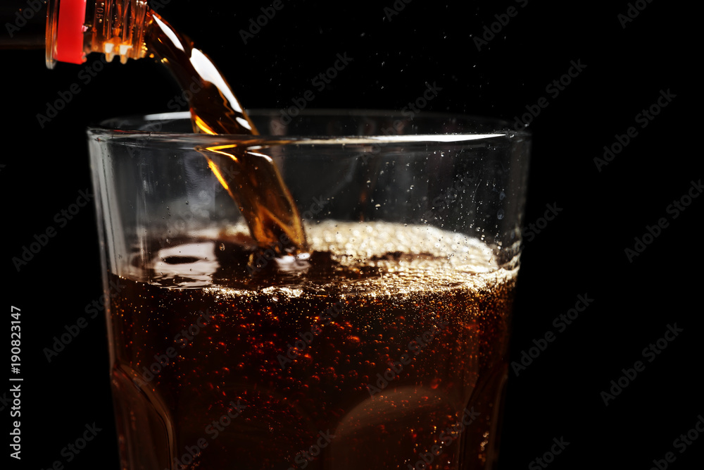 Pouring cola from bottle into glass against black background, closeup ...