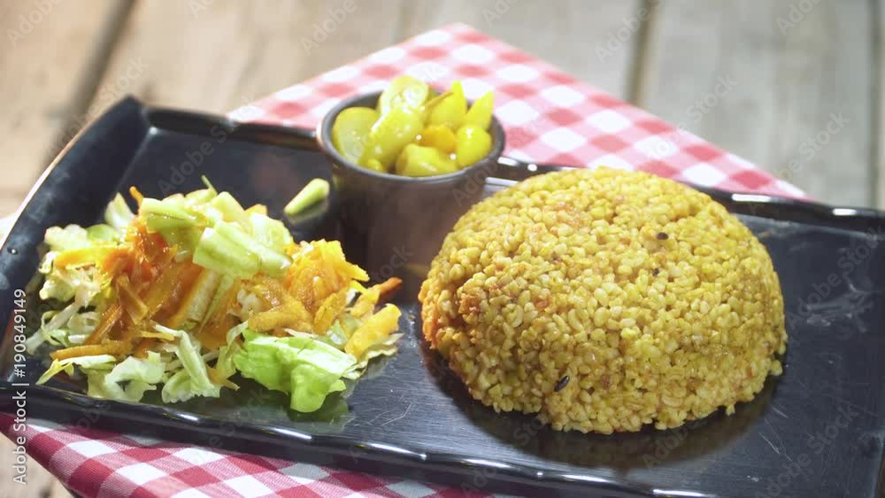 Plain bulgur rice with salad and pickles rotating on black plate in ...