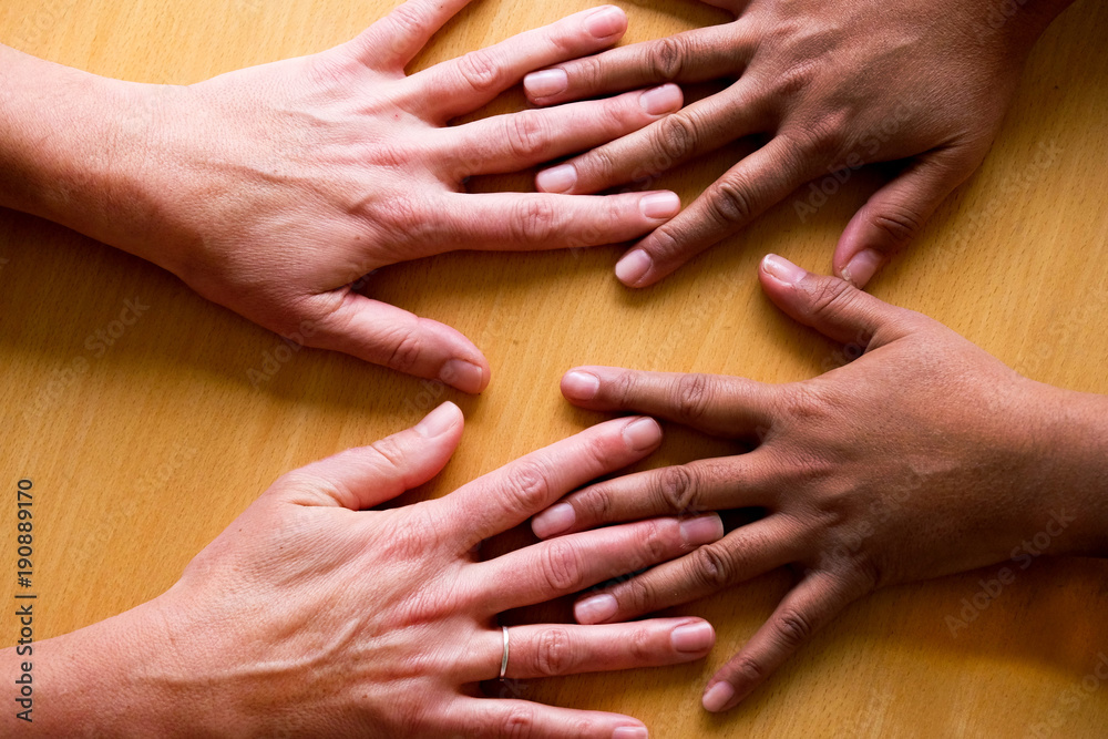 looking down on four hands, fingers spread out, lying flat on a table ...