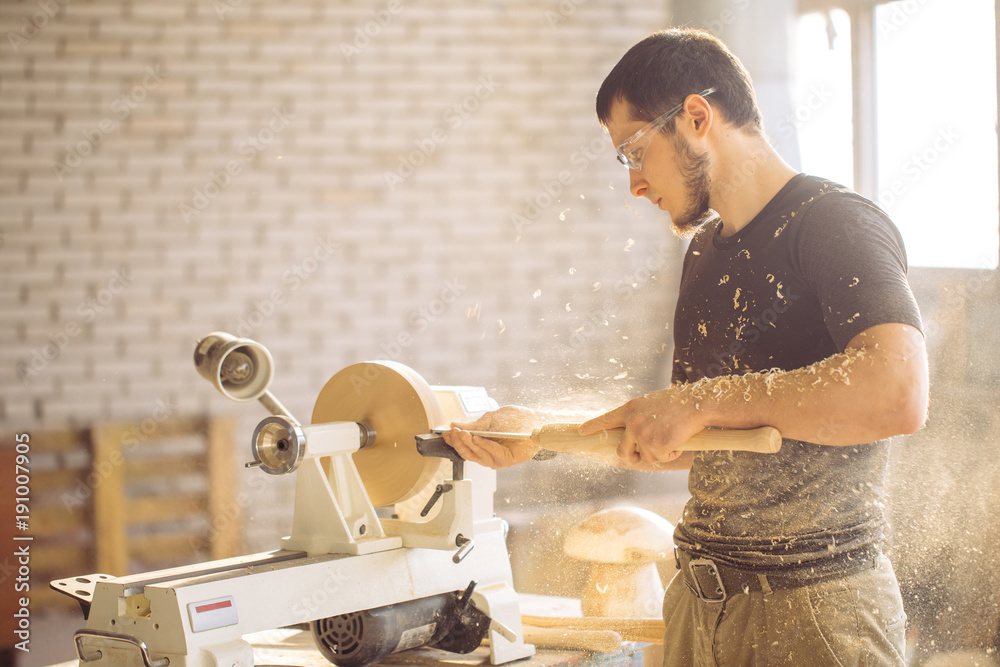 carpenter man working at small wood lathe, an artisan carves piece of ...