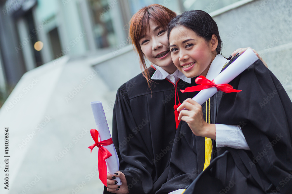 Portrait of Two happy graduated young girls in graduation gowns holding ...