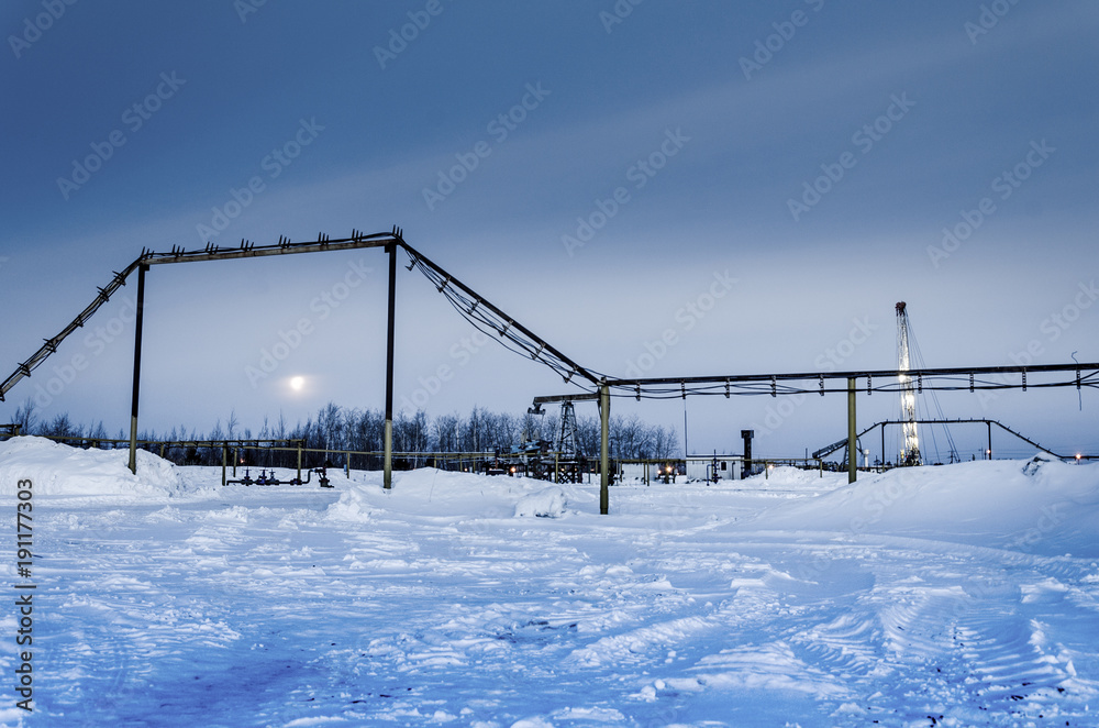 Pump jack, wellhead, pipeline and oil rig during moon eclipse in the oilfield. Winter period ...