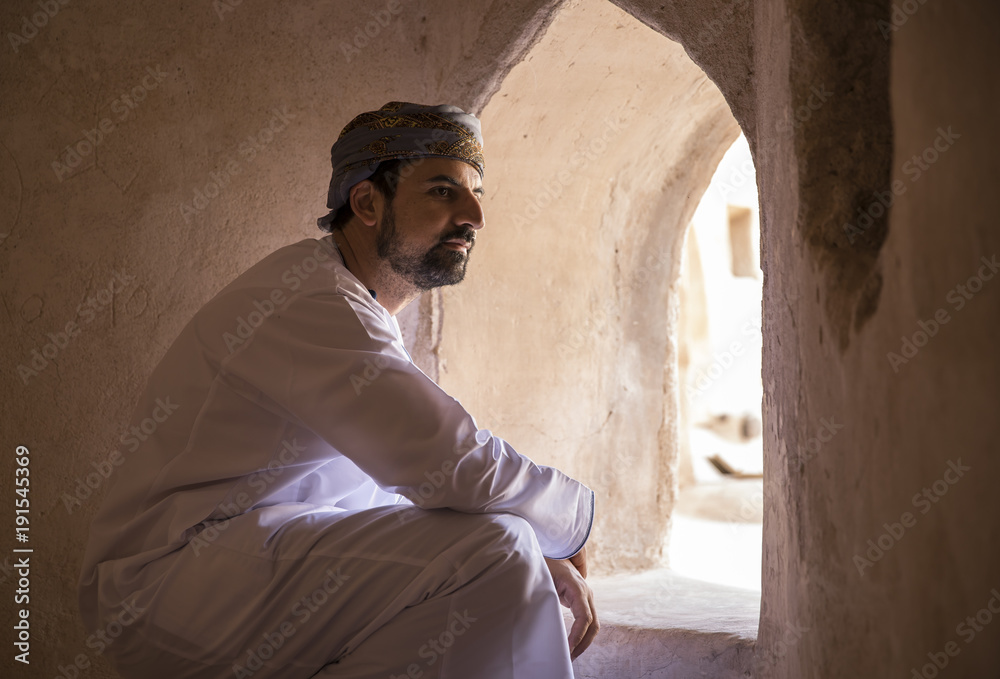 arab man in traditional omani outfit looking out of a window in an old ...