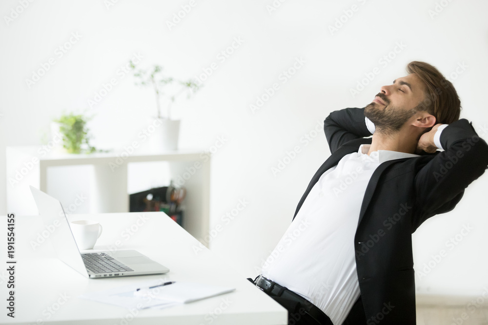 Successful young businessman in suit relaxing at workplace with laptop ...