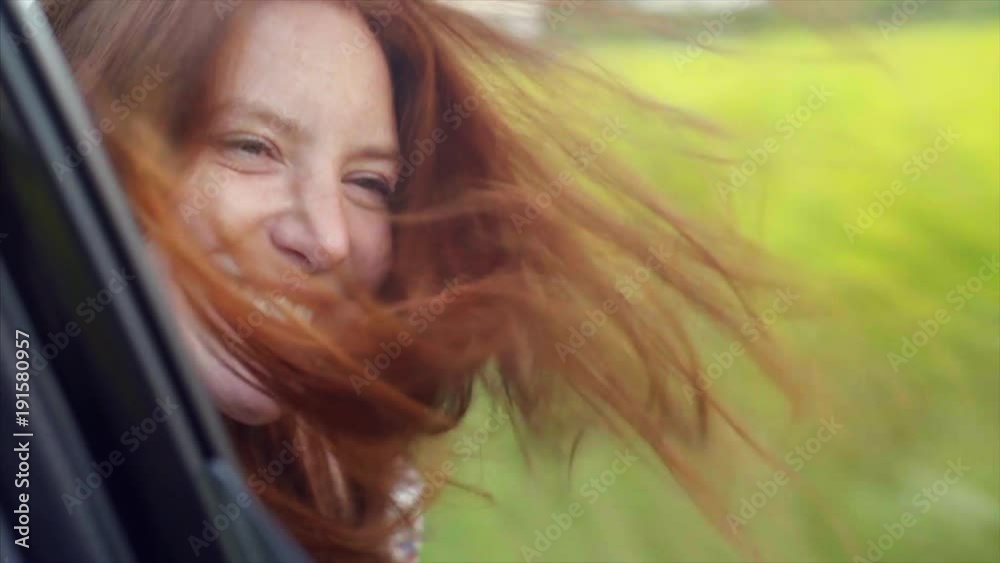 Young woman out of car window, close-up portrait happy and enjoing wind ...