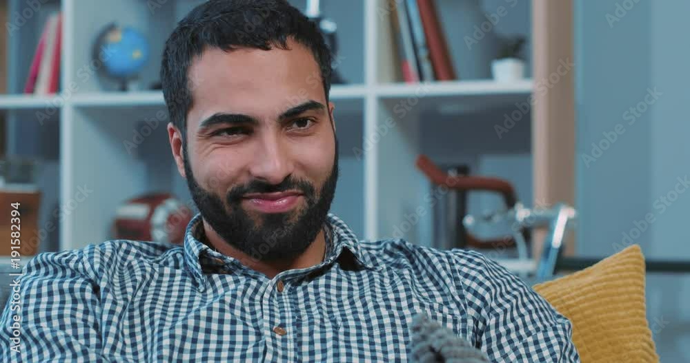 Close up face young smiling attractive man drinking beer watching tv ...