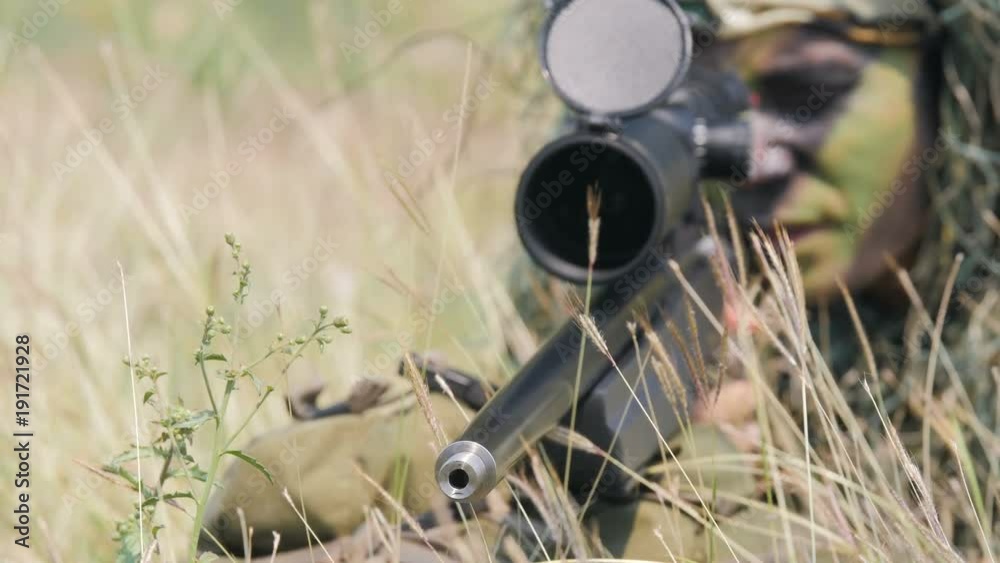 Army sniper wearing disguise camouflage suit lying and aiming in grass ...