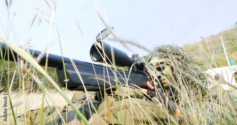 Army sniper wearing disguise camouflage suit lying and aiming in grass ...