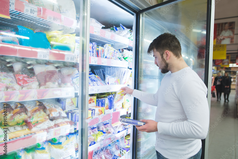A man chooses frozen foods from shelves in a refrigerator in a ...