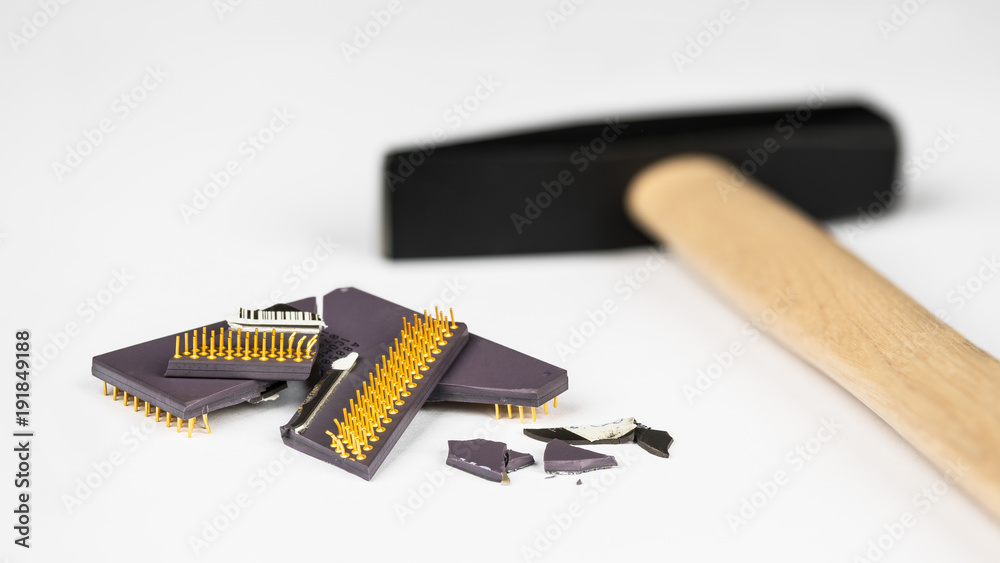 Broken computer processor on blurred background with hammer. Fragments of the central processing ...