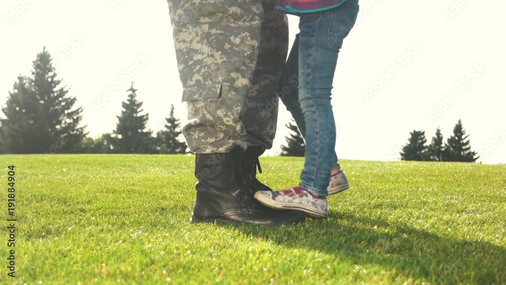 Soldier legs and little girl legs playing together. Feet of a man in army uniform and daughter ...