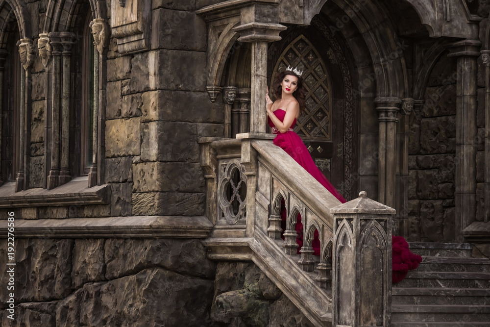 A beautiful woman, a queen in a red dress, stands on the background of ...