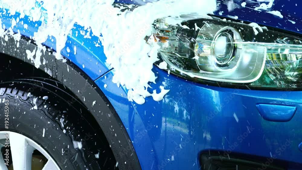 Man spraying chemical cleaning white foam on the blue compact car and ...