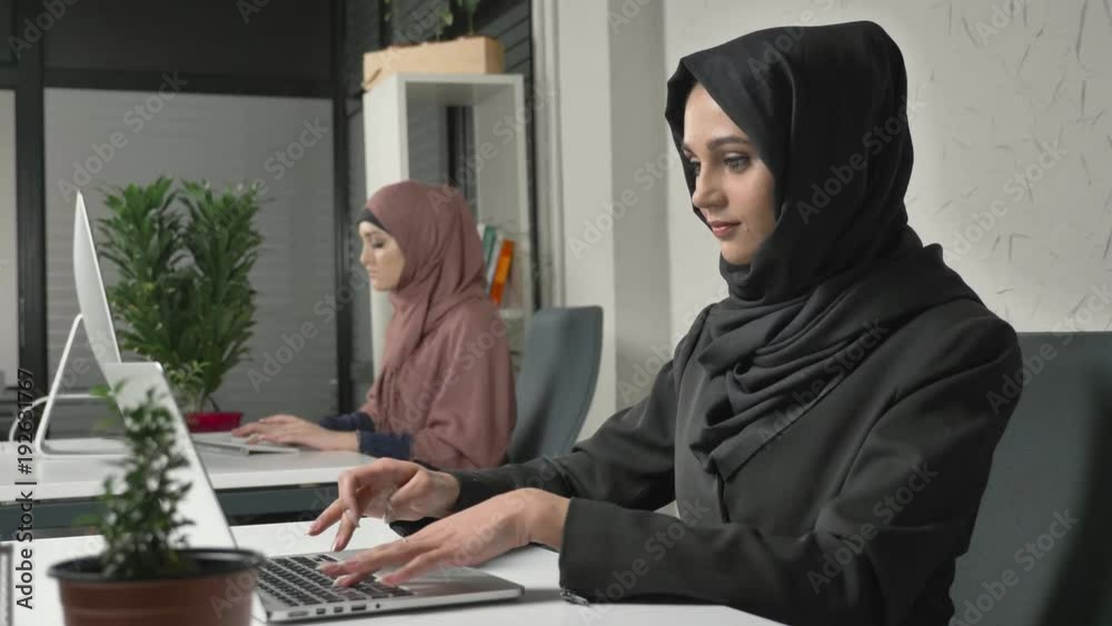 Two Muslim girls in hijabs work in the office, type on the keyboard ...