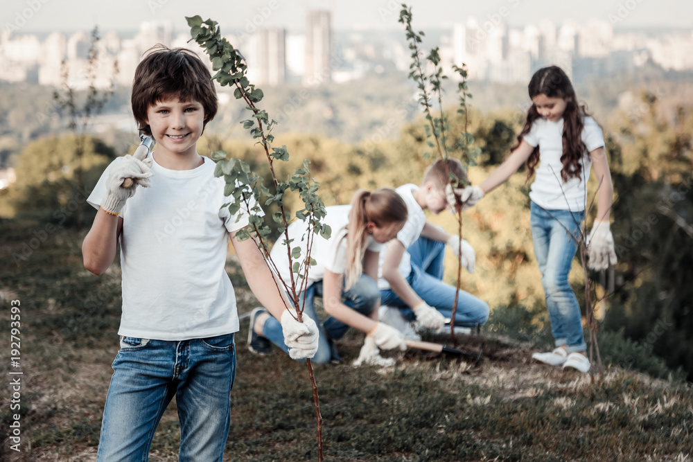 Green planet. Happy cute positive boy smiling and holding a young tree ...