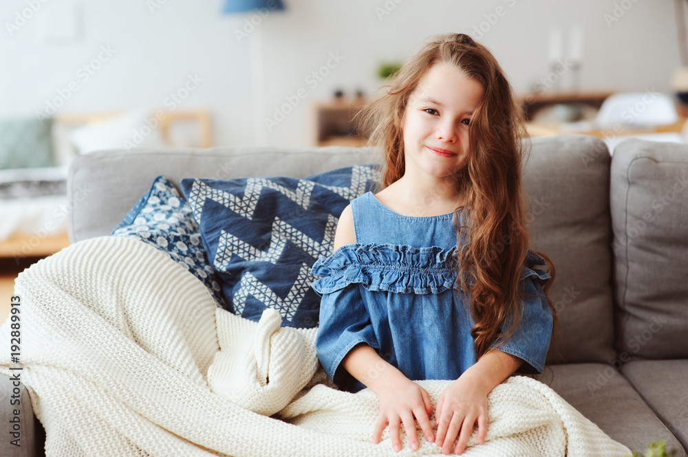 cute little child girl relaxing at home, sitting on couch, wrapped in ...
