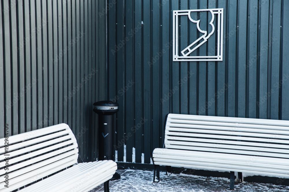 Smoking area with ash bin and two white benches for relaxation. Sign on ...