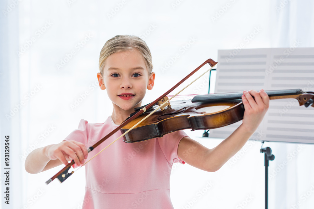 portrait of cute little child in pink dress playing violin at home ...