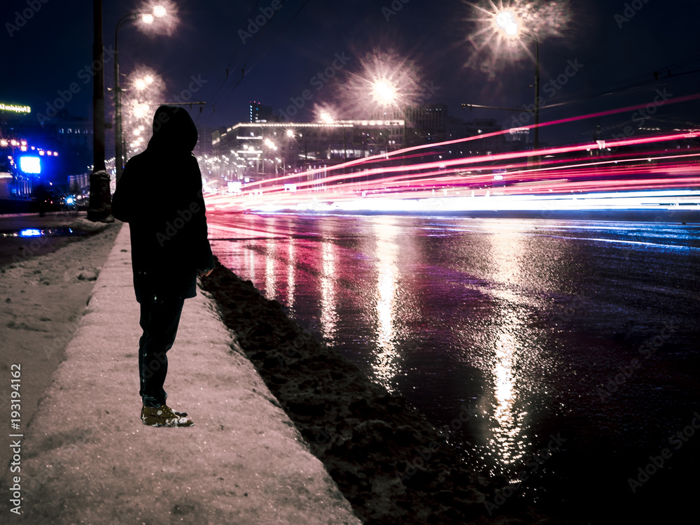 young man standing near the traffic on the highway, long exposure shot ...