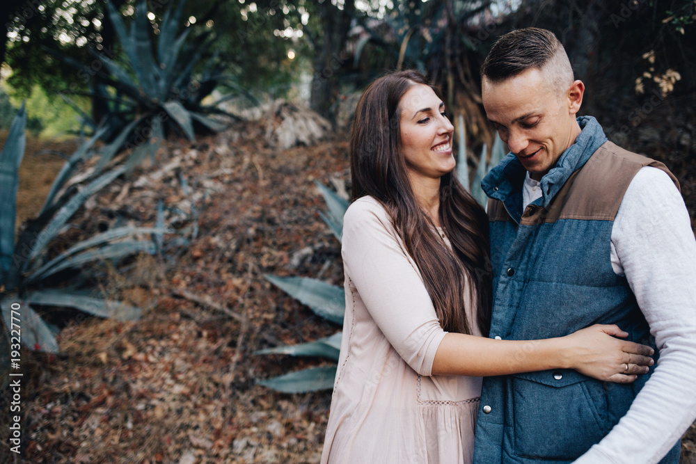 Wife wrapping arms around husbands waist with husband looking down ...