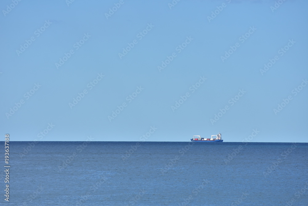 Container ship with cargo alone on dark blue ocean with light blue sky ...