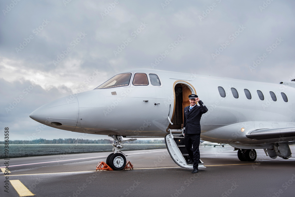 Full length portrait of cheerful aviator leaving stairs of aircraft at ...