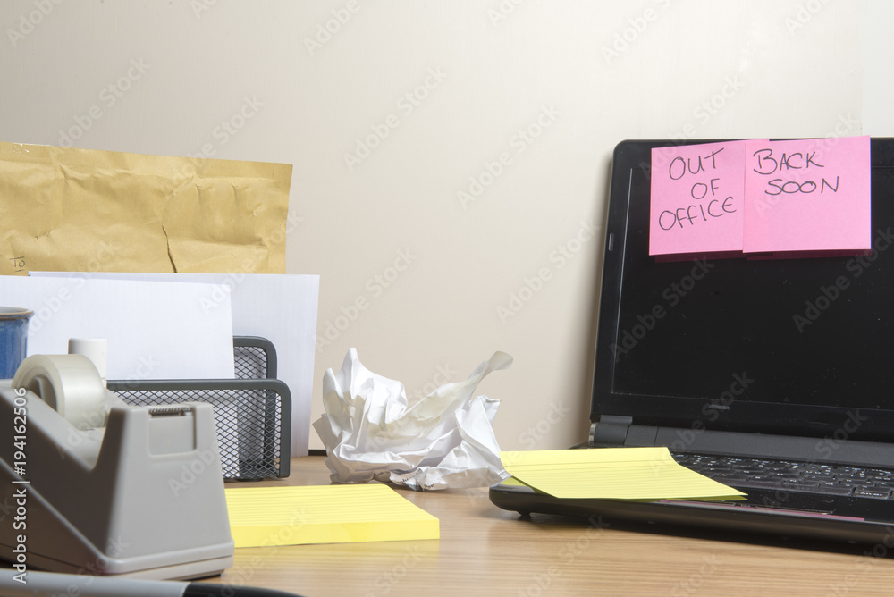 Out of office, back soon message left on a laptop on a messy office ...