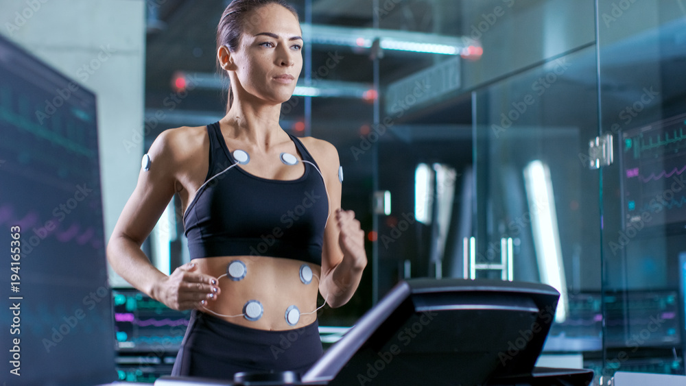 Beautiful Woman Athlete Runs on a Treadmill with Electrodes Attached to ...