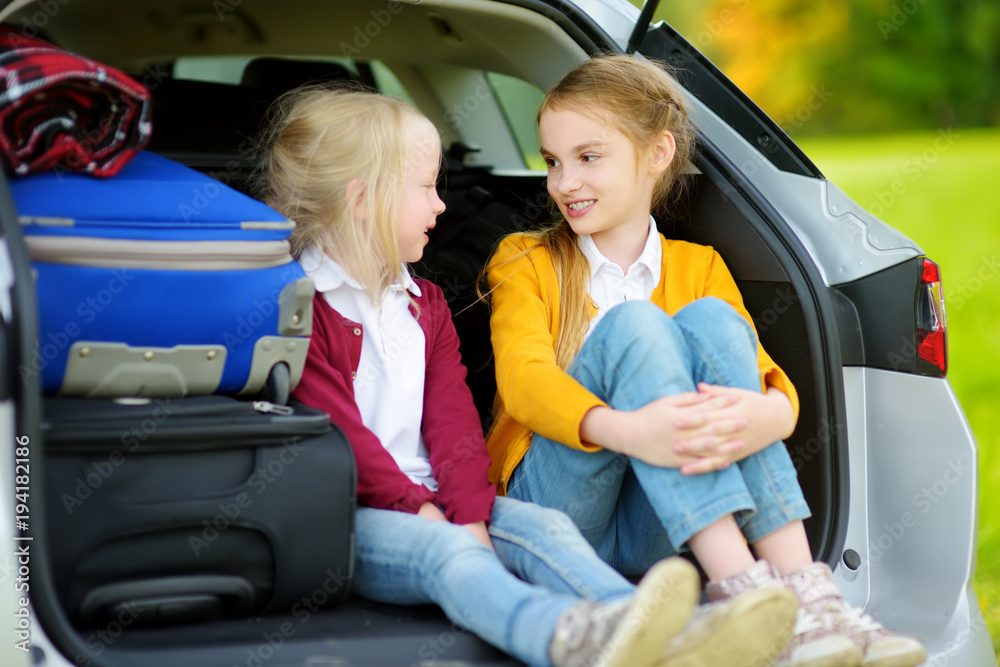 Two adorable little girls sitting in a car before going on vacations ...