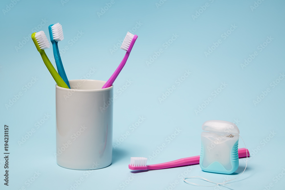 Colorful toothbrushes in mug and dental floss on light blue background ...