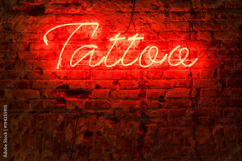 Glowing red neon signboard word tattoo on a brick dark background ...