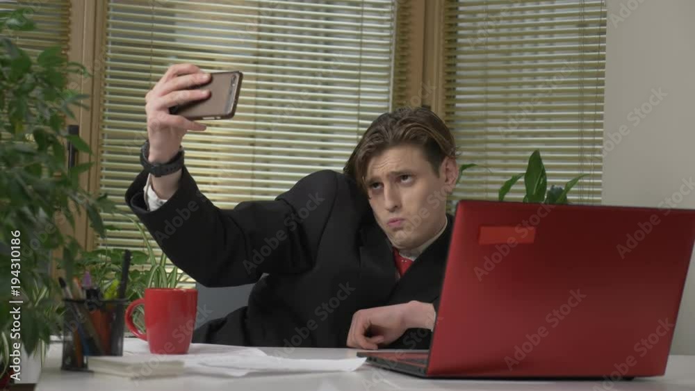 Young man in a suit is sitting in the office and making a selfie. Makes ...