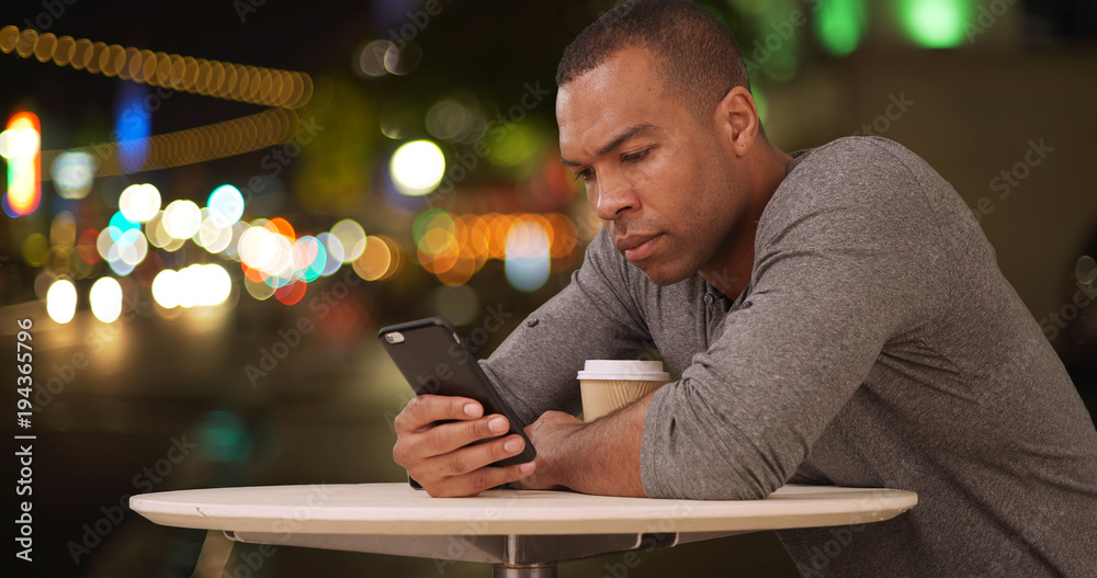 Black man sitting alone at outdoor cafe drinking coffee at night and ...