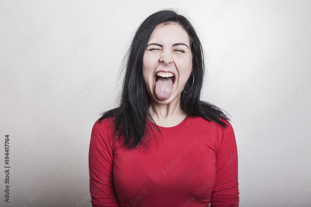 Frau in rotem Shirt mit schwarzen langen Haaren streckt die Zunge raus ...