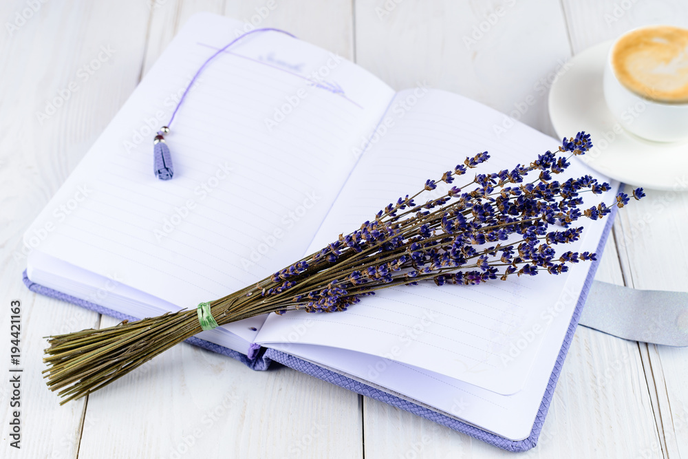 Purple notebook, cup of coffee and flowers on light wooden background ...