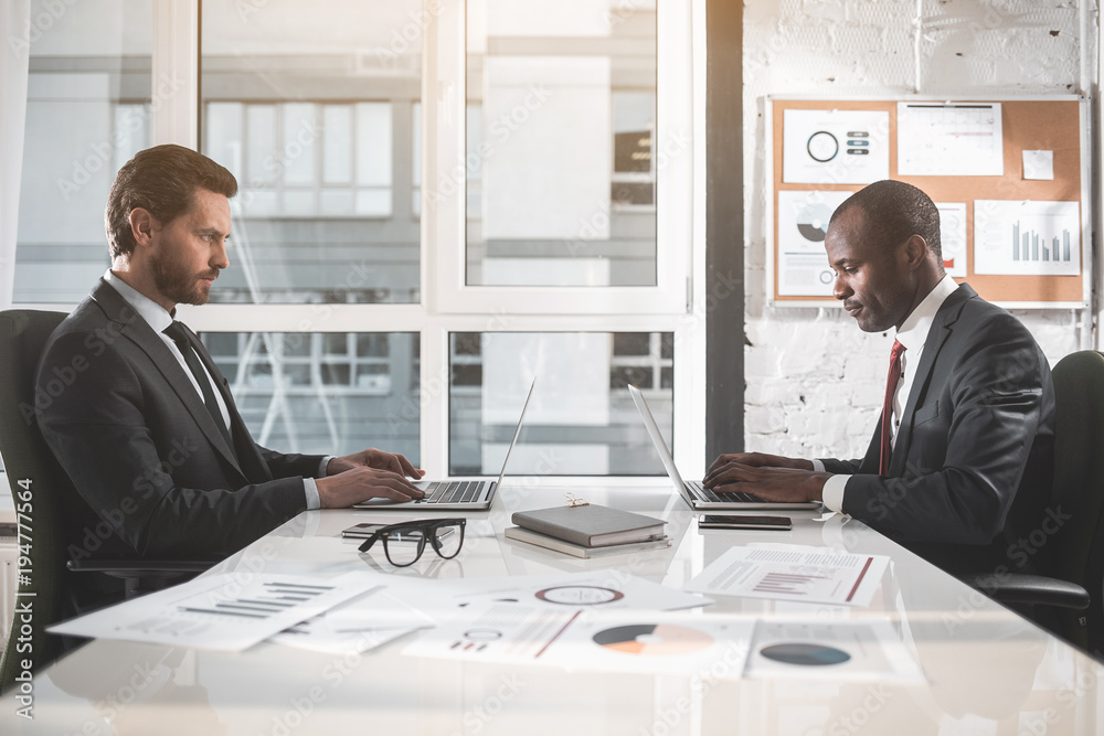 Too busy. Profile of two serious businessmen are sitting at table ...