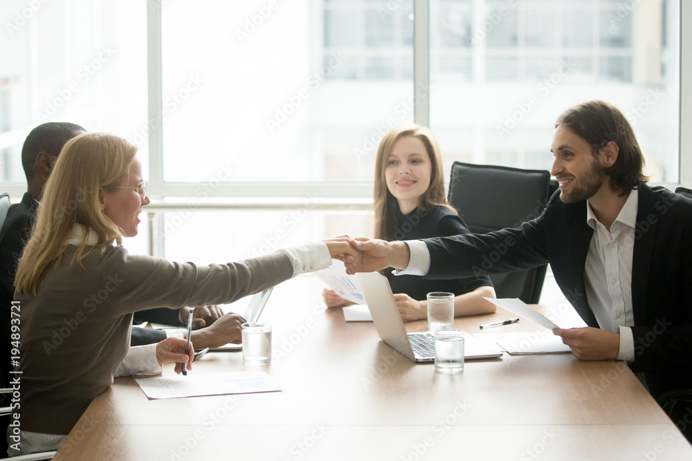 Smiling businessman and businesswoman shaking hands over conference ...
