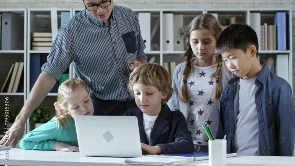 Four primary school children doing group task on laptop computer under ...