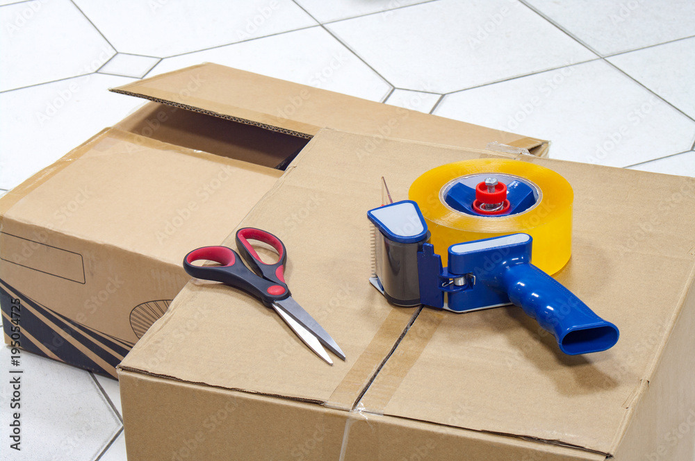 Packing tape dispenser and the scissors on the cardboard box. Stock ...