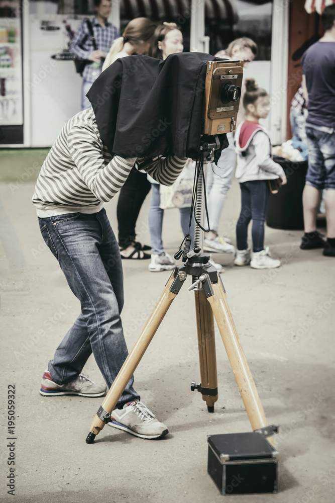 Photographer with antiquity vintage wooden camera under dark cloth cape ...