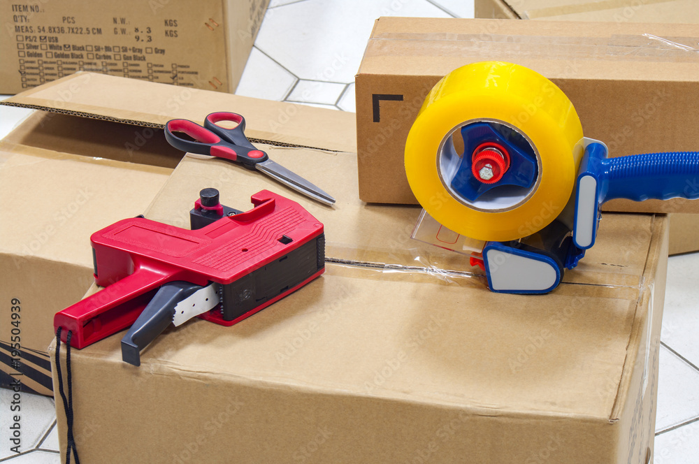 Packing tape dispenser, scissors and label gun on the cardboard box ...